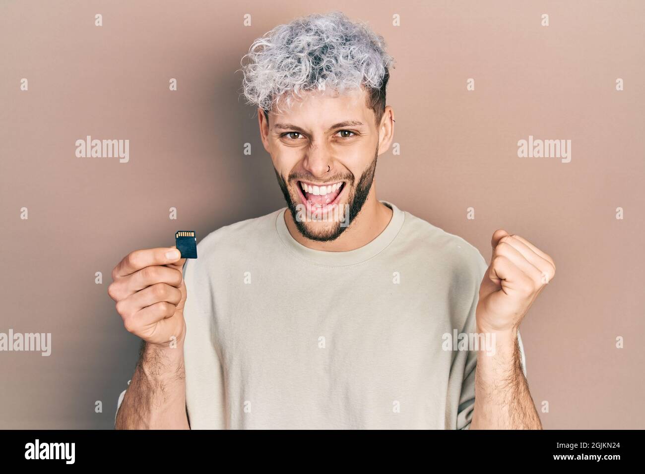 Young hispanic man with modern dyed hair holding sdxc card screaming ...