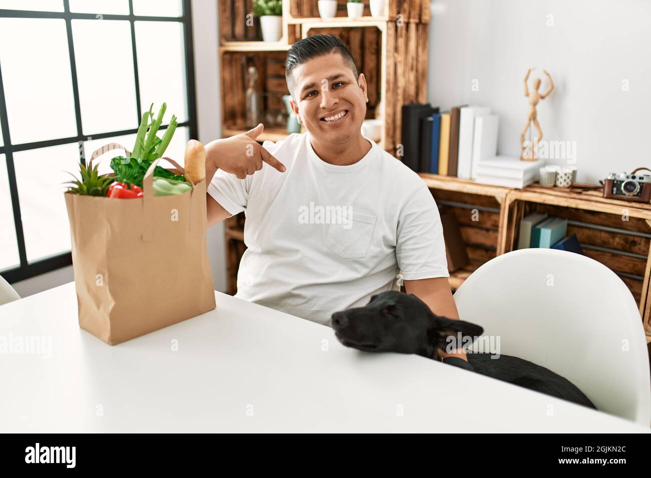 Young hispanic man sitting with paper bag with groceries pointing ...