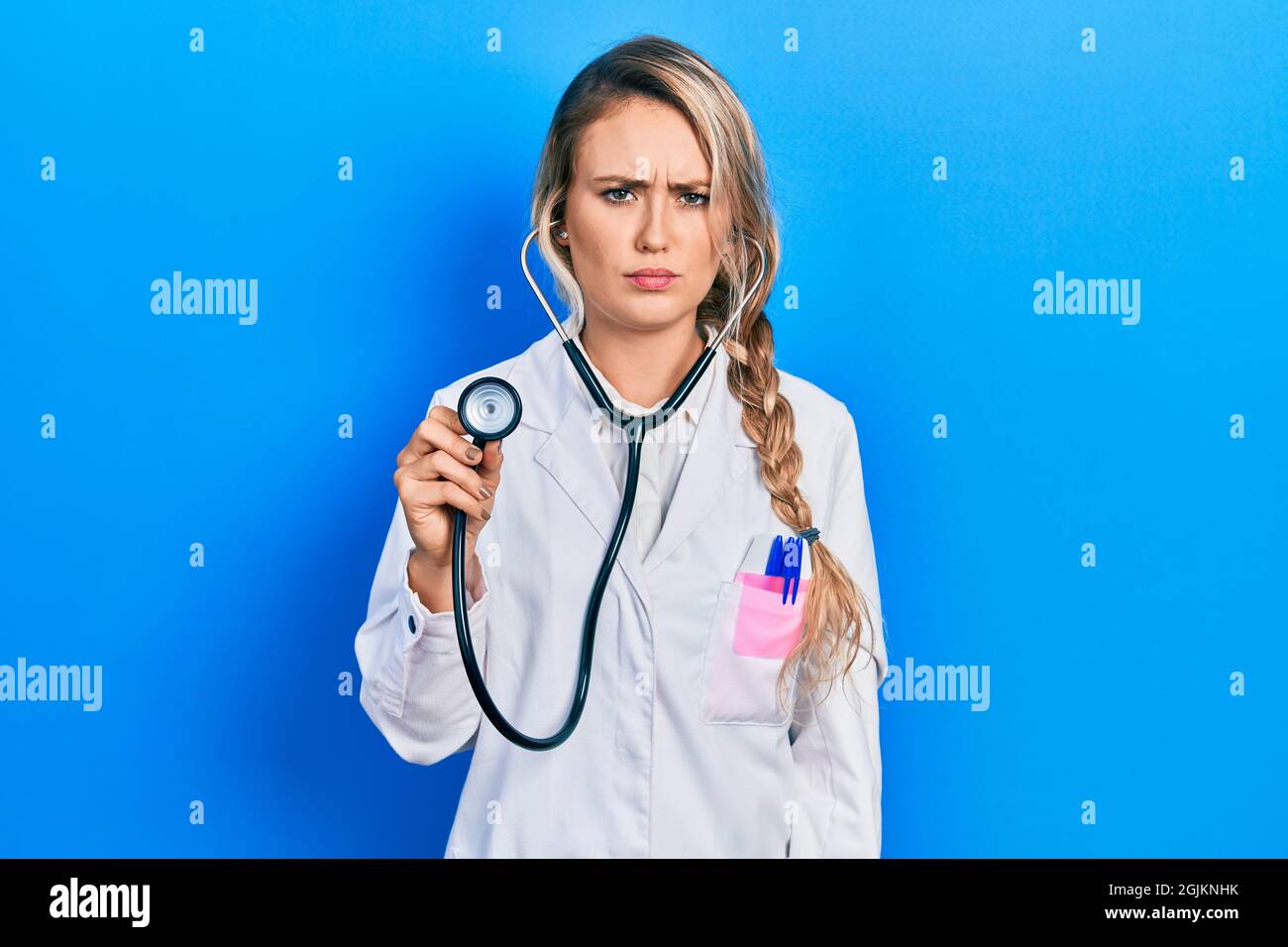 Beautiful young blonde doctor woman holding stethoscope skeptic and ...