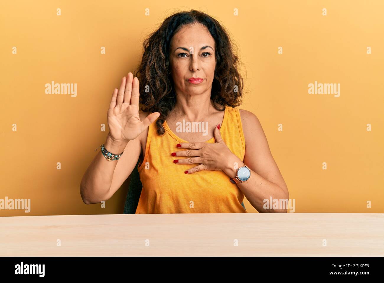 Beautiful middle age woman wearing casual clothes sitting on the table ...