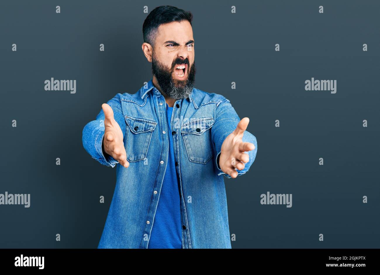 Hispanic man with beard with open arms doing hug gesture angry and mad ...