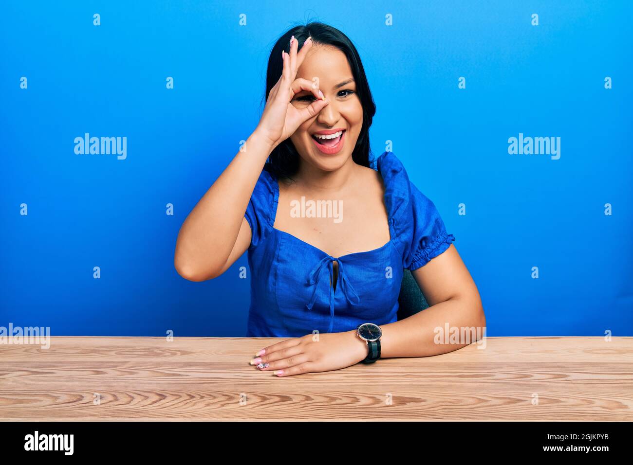 Beautiful hispanic woman with nose piercing sitting on the table doing ...