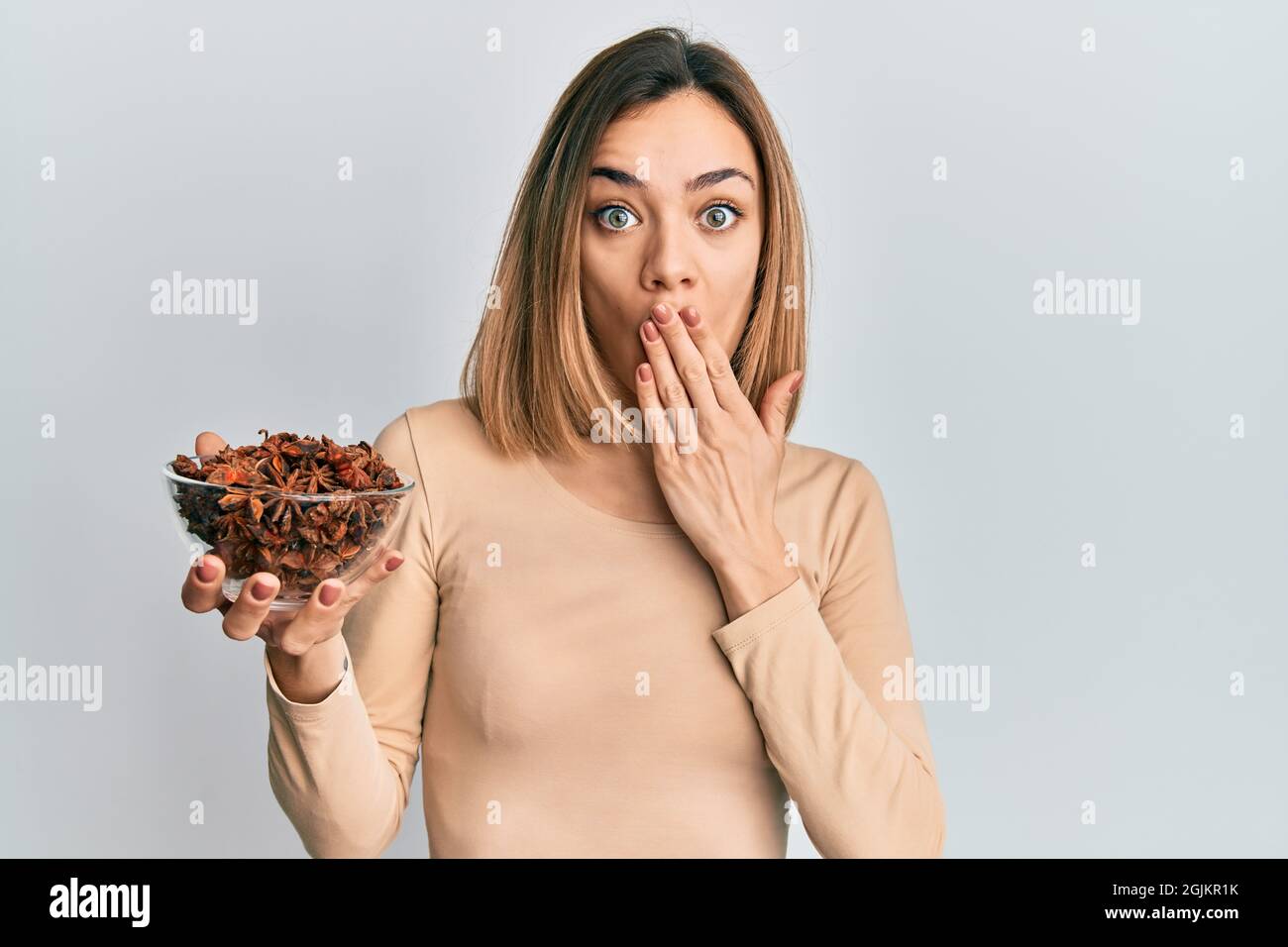 Young caucasian blonde woman holding bowl of star anise covering mouth ...