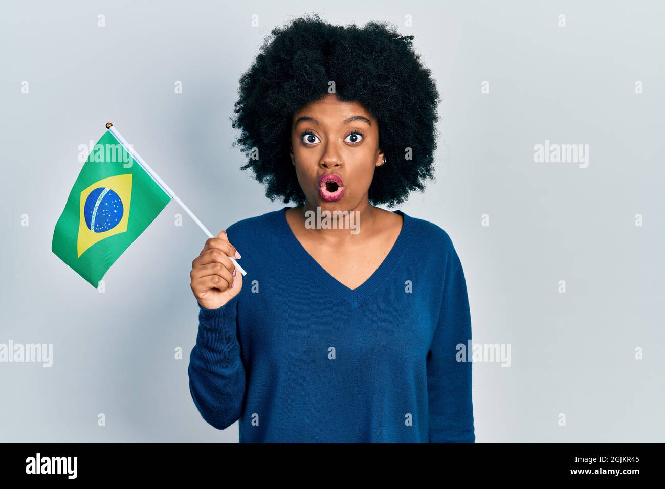 Young african american woman holding brazil flag scared and amazed with ...