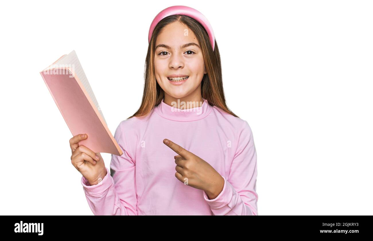 Beautiful brunette little girl reading a book smiling happy pointing ...