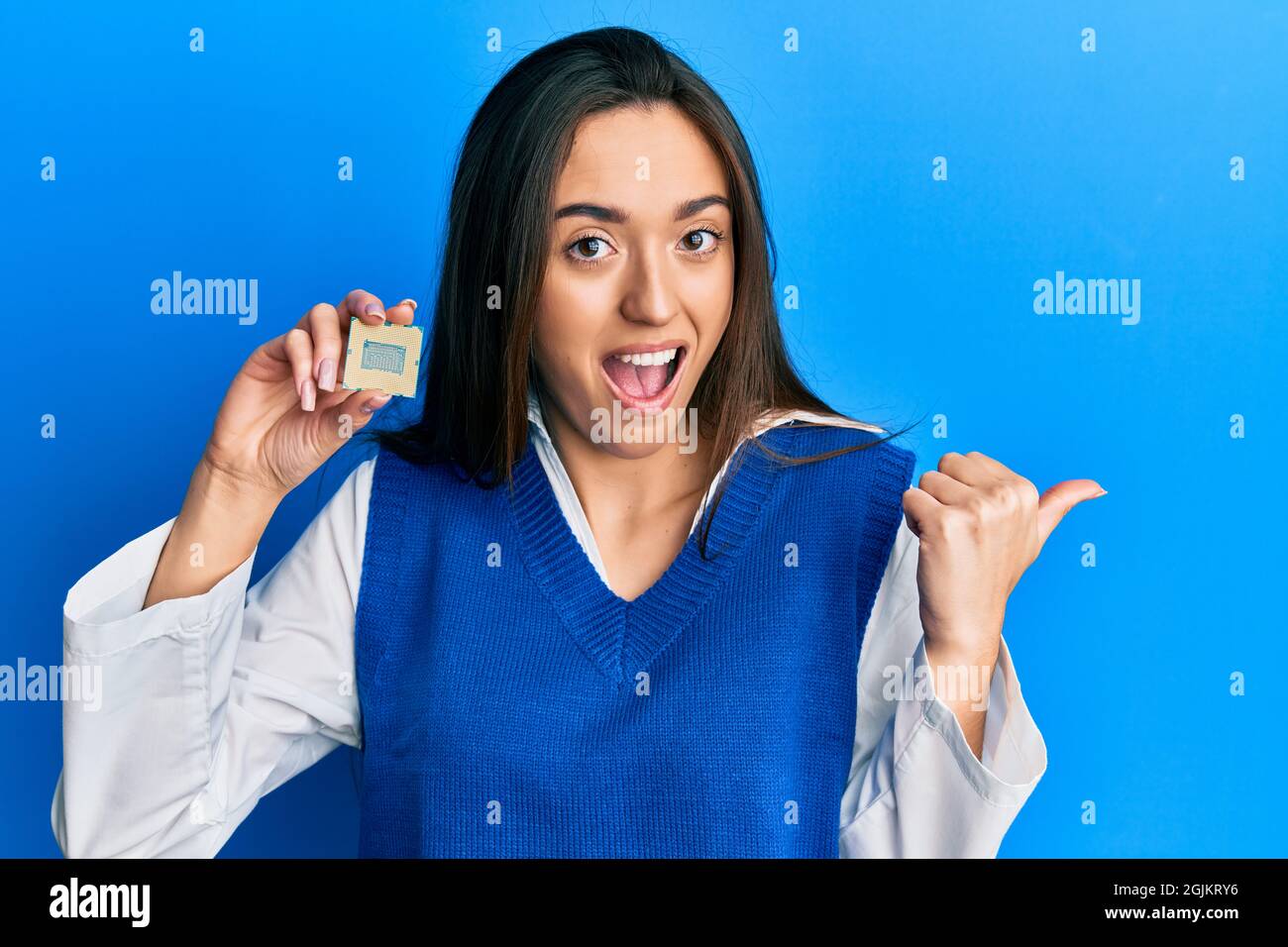 Young hispanic girl holding cpu computer processor pointing thumb up to ...