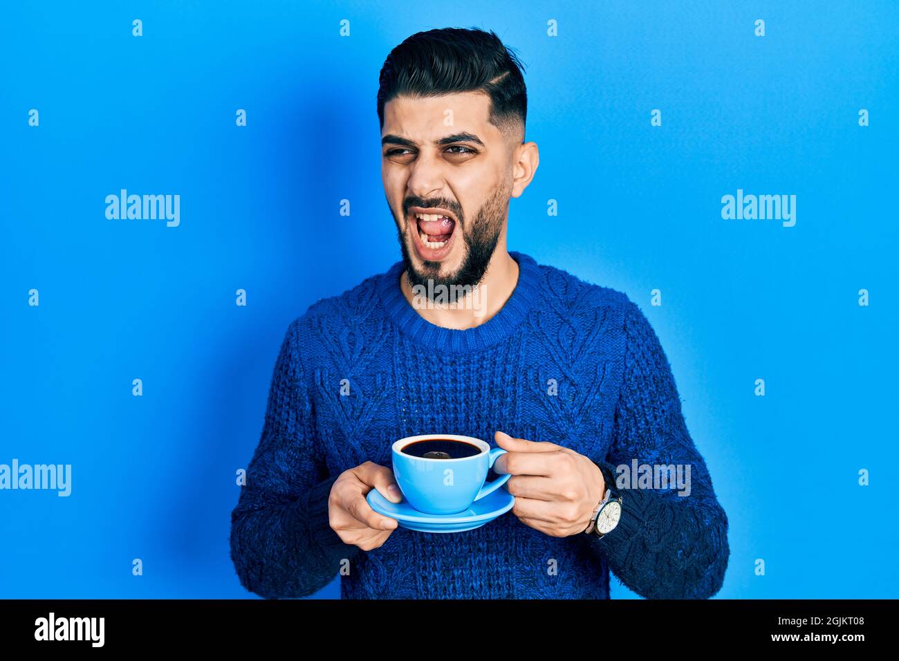 Handsome man with beard drinking a cup of coffee angry and mad ...
