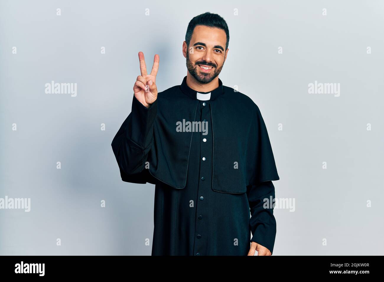 Handsome hispanic man with beard wearing catholic priest robe smiling ...