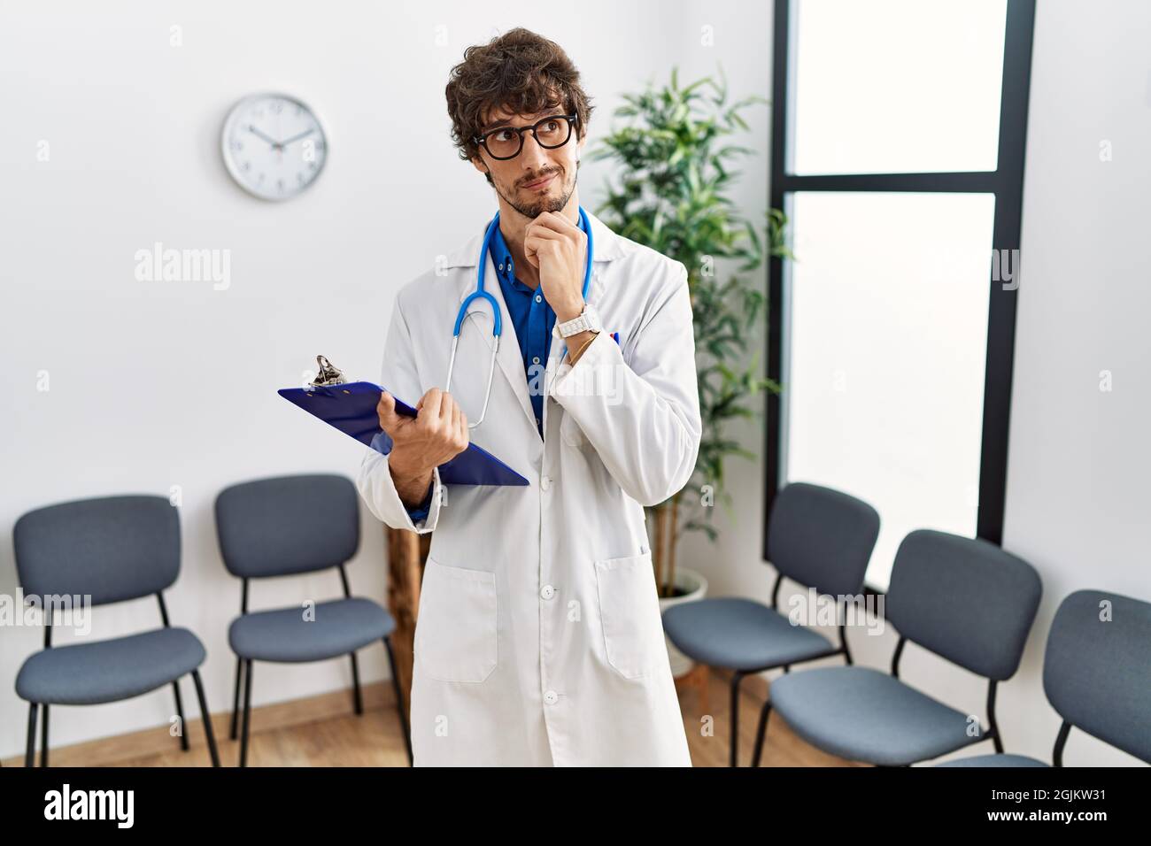 Young hispanic doctor man at waiting room with hand on chin thinking ...