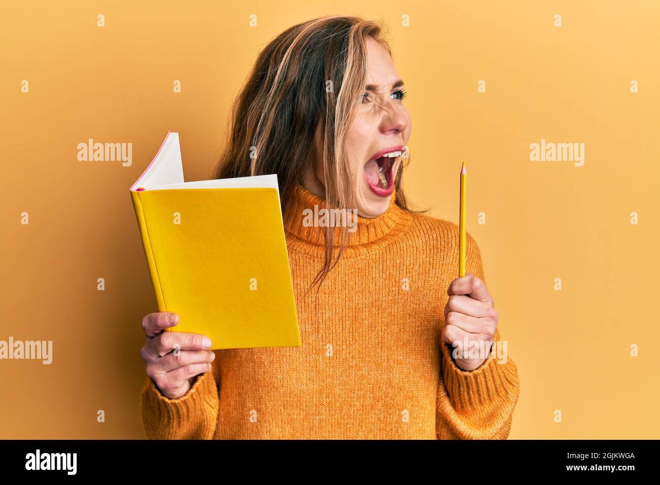 Young blonde woman holding book and pencil angry and mad screaming ...
