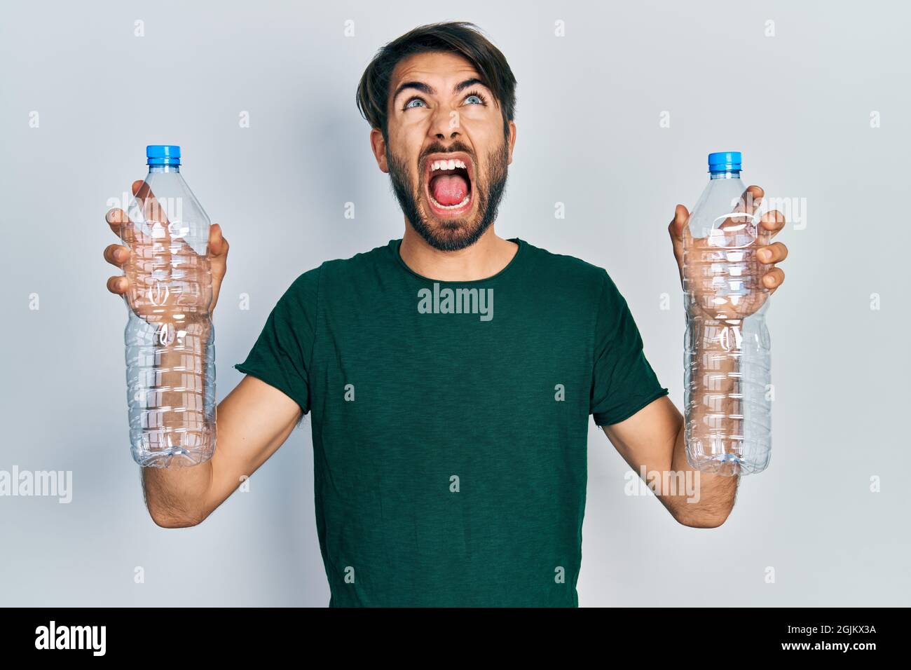 Young hispanic man holding recycling plastic bottles angry and mad ...