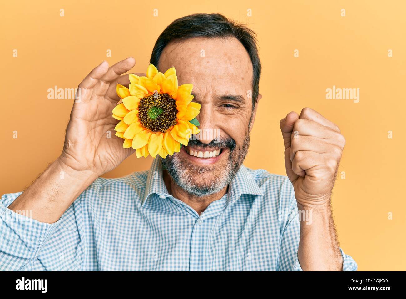 Middle age hispanic man holding sunflower over eye screaming proud ...