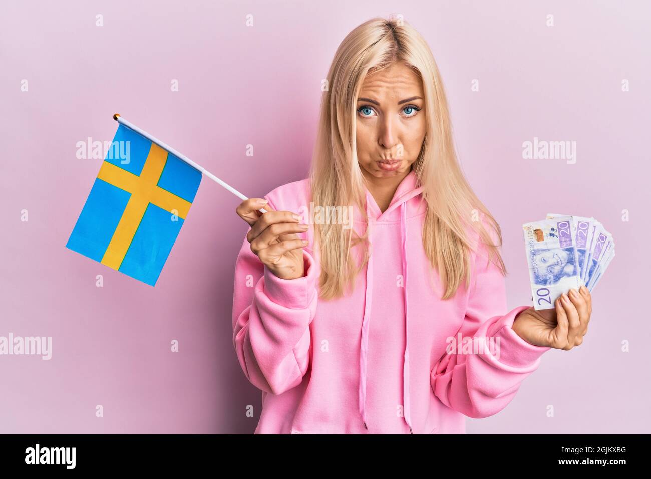 Young blonde woman holding sweden flag and krone banknotes depressed ...