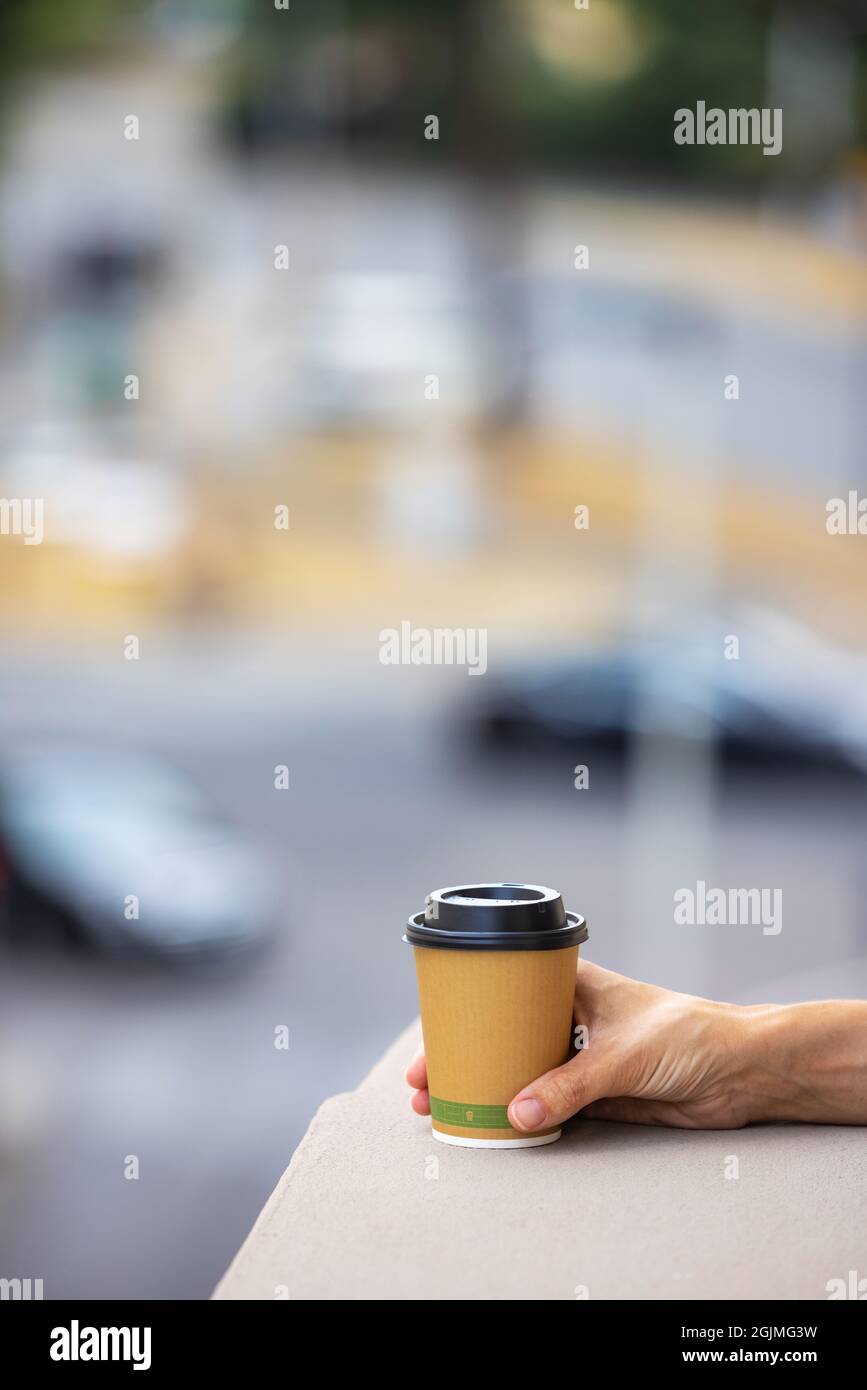 Hands holding a single use paper coffee cup. Young woman in a balcony ...