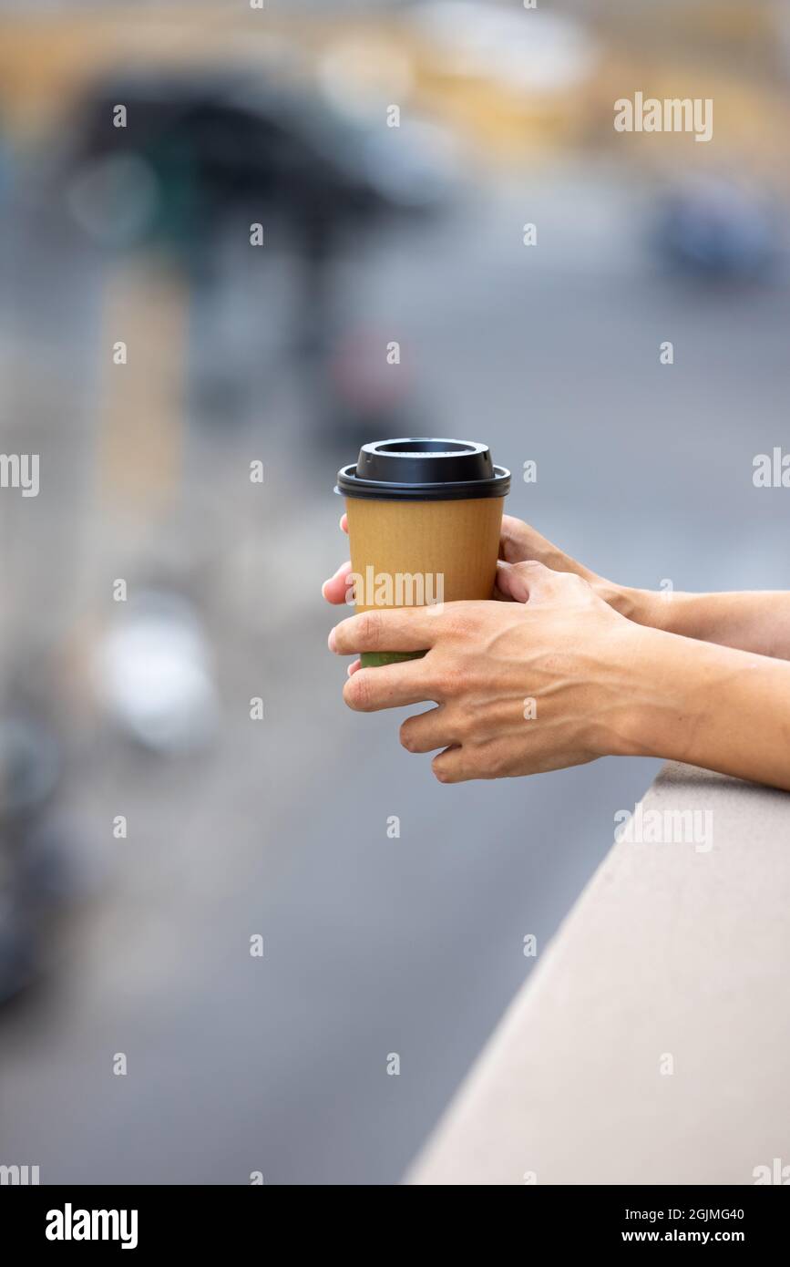 Hands holding a single use paper coffee cup. Young woman in a balcony ...