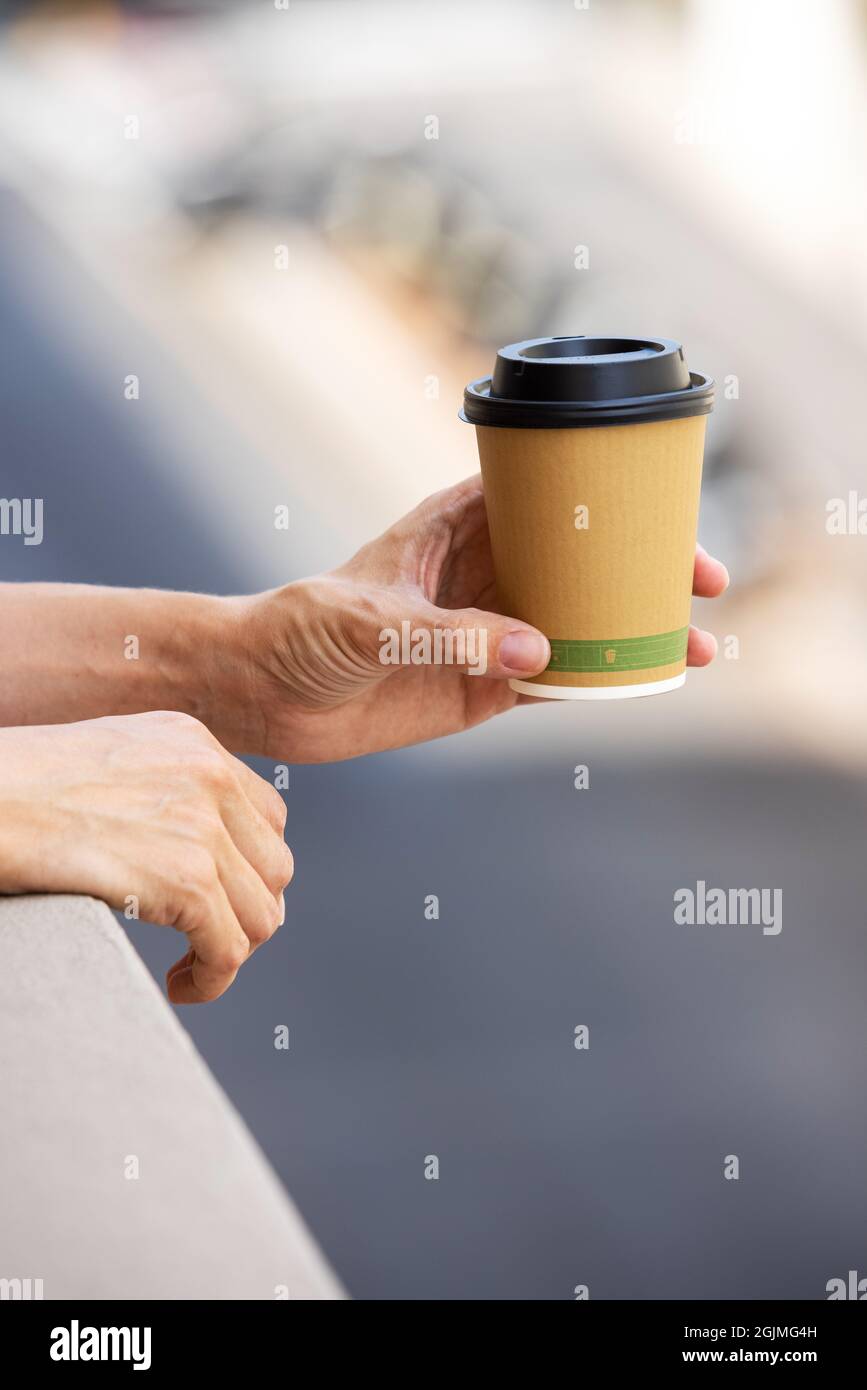 Hands holding a single use paper coffee cup. Young woman in a balcony ...