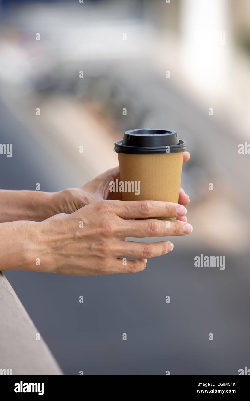 Hands holding a single use paper coffee cup. Young woman in a balcony ...