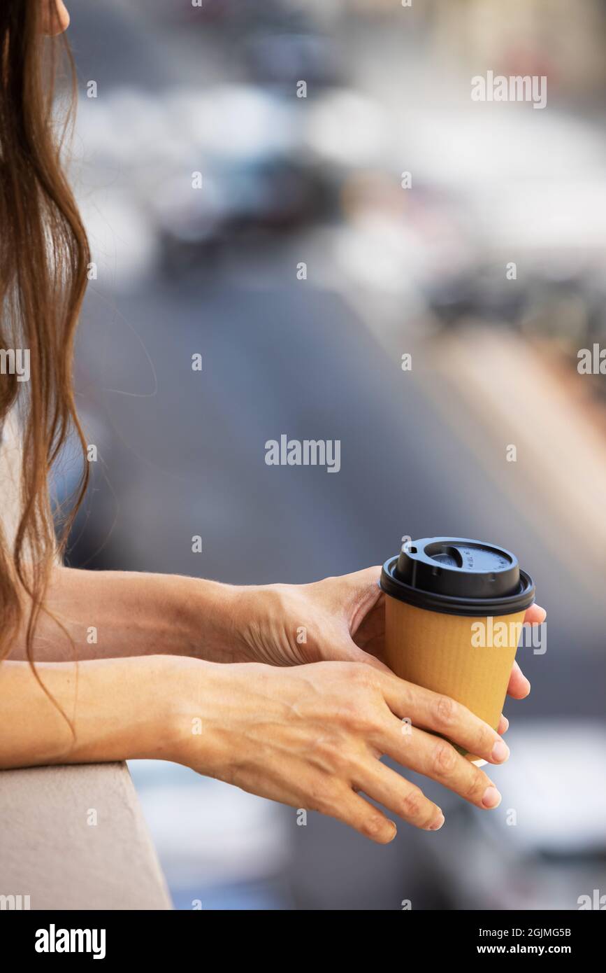 Hands holding a single use paper coffee cup. Young woman in a balcony ...