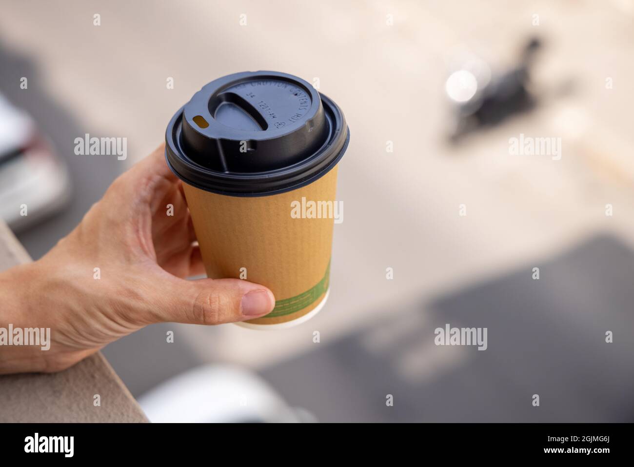 Hands holding a single use paper coffee cup. Young woman in a balcony ...