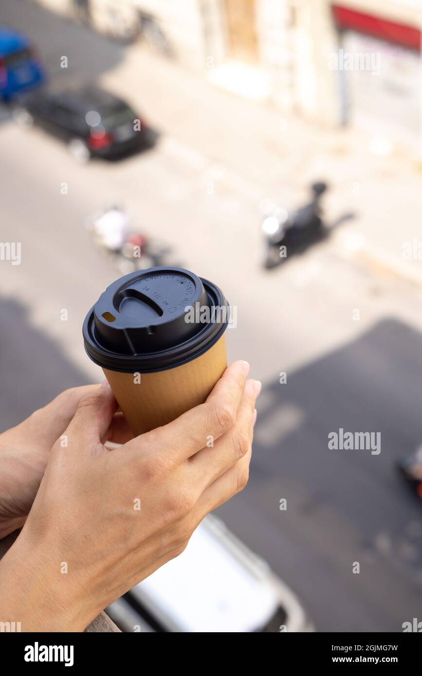 Hands holding a single use paper coffee cup. Young woman in a balcony ...