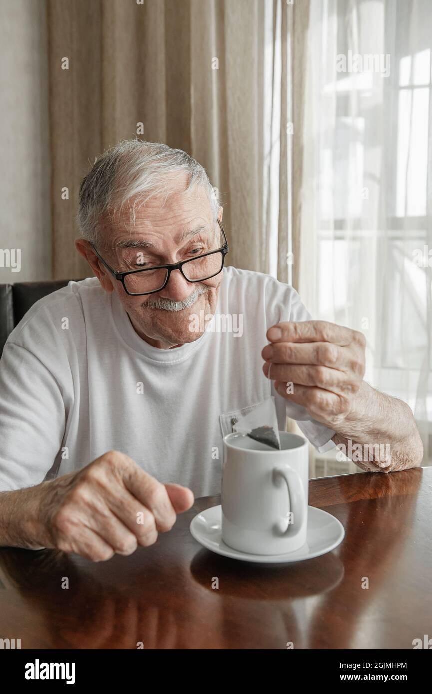 gray-haired, cheerful old man is brewing a tea bag in a cup. Portrait ...