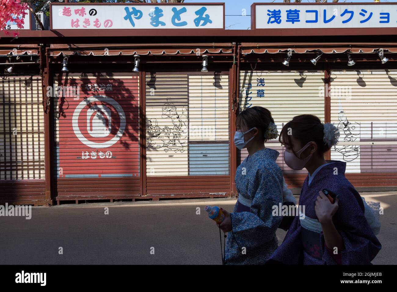 Two young women, wearing kimono and face mask , walk past shuttered ...