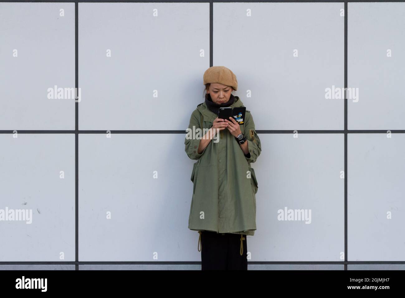 A Japanese woman, wearing a beret, using a smartphone against a white ...