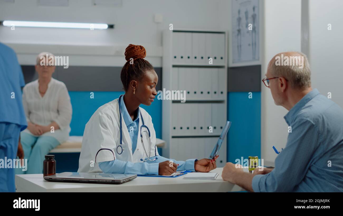 Young medic explaining x ray result to old man at desk in healthcare ...