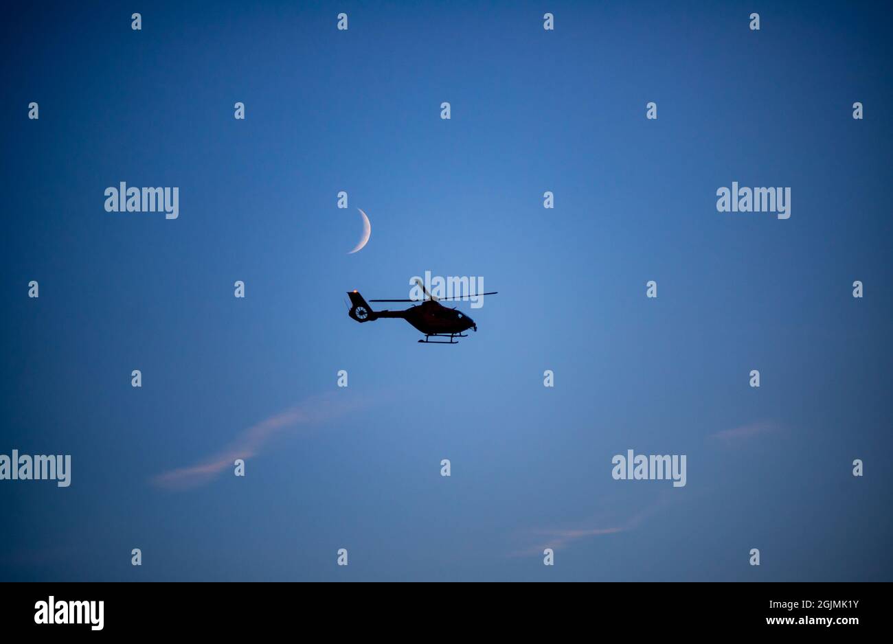 A rescue helicopter flies under the crescent moon early in the evening ...