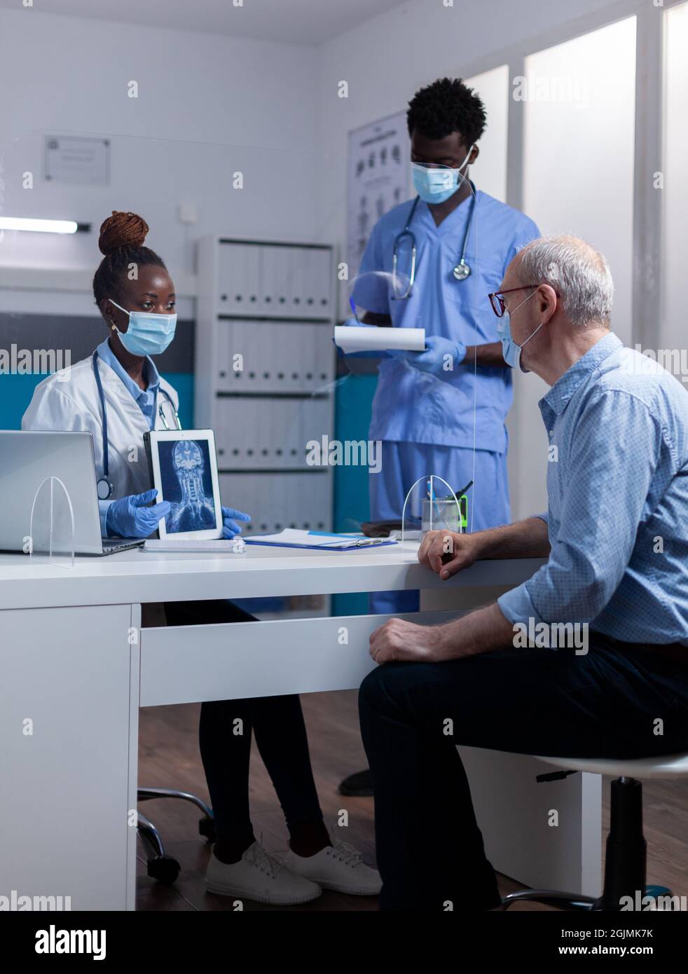 Medical team of black people talking to elderly patient sitting at desk ...