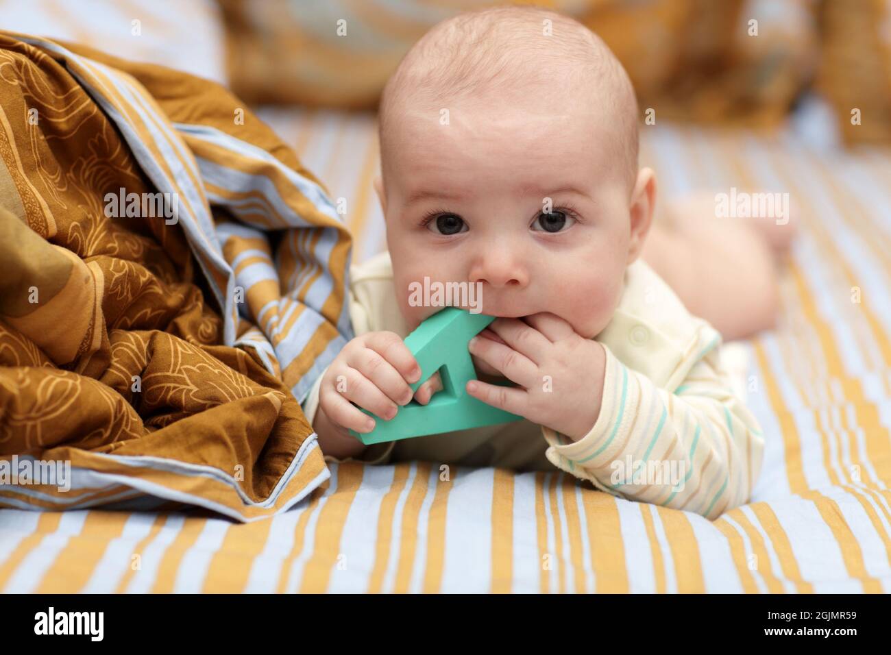 A baby biting letter A on a bed at home Stock Photo - Alamy