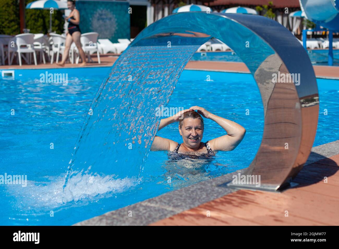 Woman swims in blue water of pool. Blonde is resting at waterfall of ...