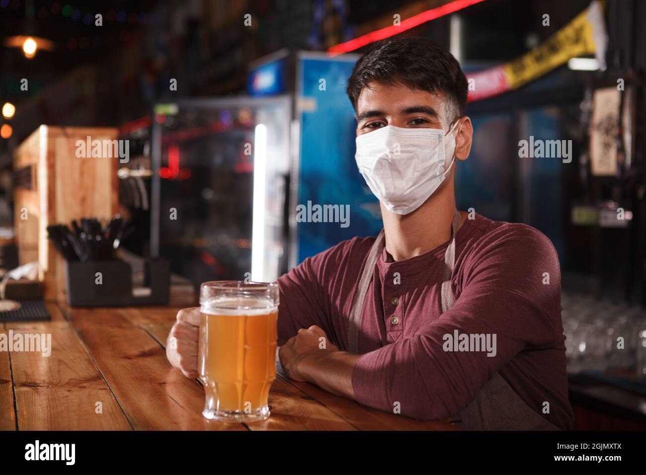 Young brewer wearing medical face mask, serving beer at his bar during ...