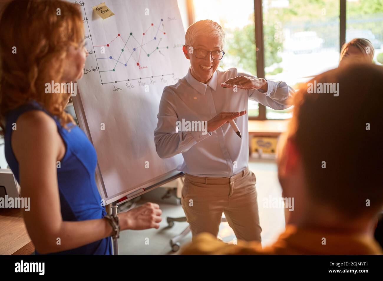 An elderly female boss enjoys explaining a graph to her colleagues in a ...