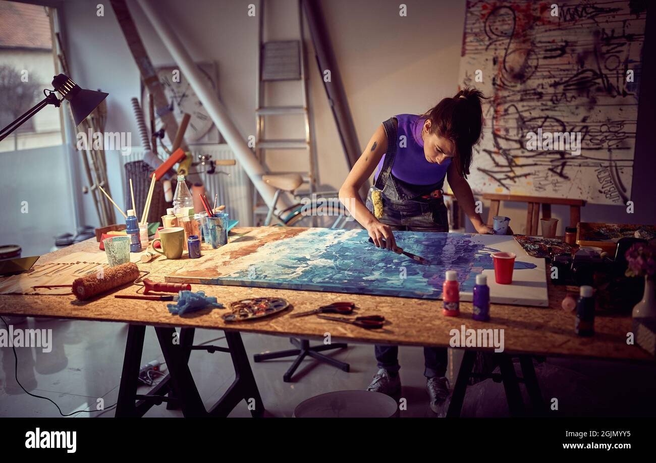 A young female artist is focused while working on a painting in a ...