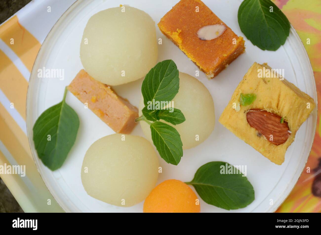 Plate of yellow gram flour sweets, syrup filled ball, brown condensed ...