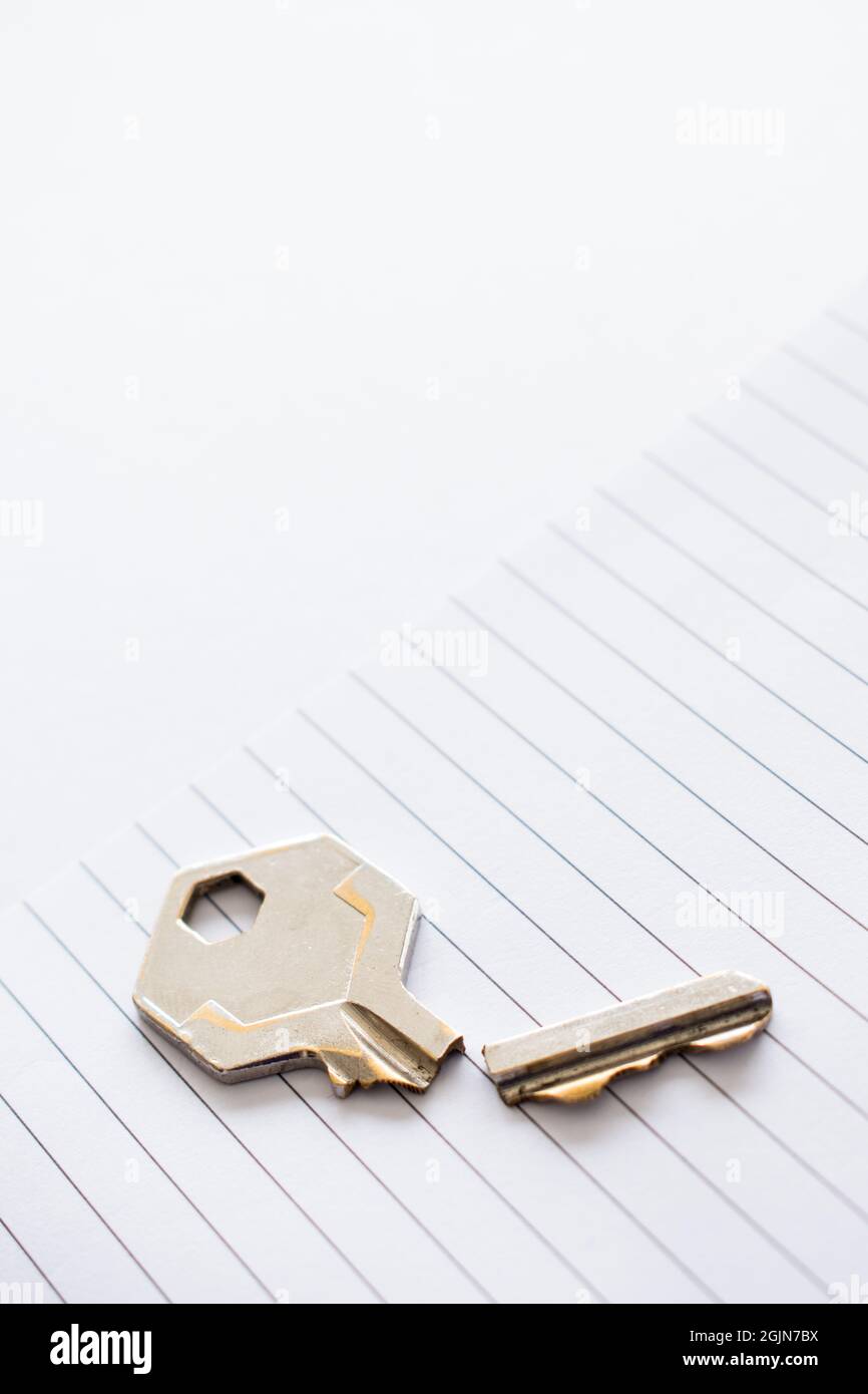 Vertical shot of a broken key on a lined paper, with a white background ...