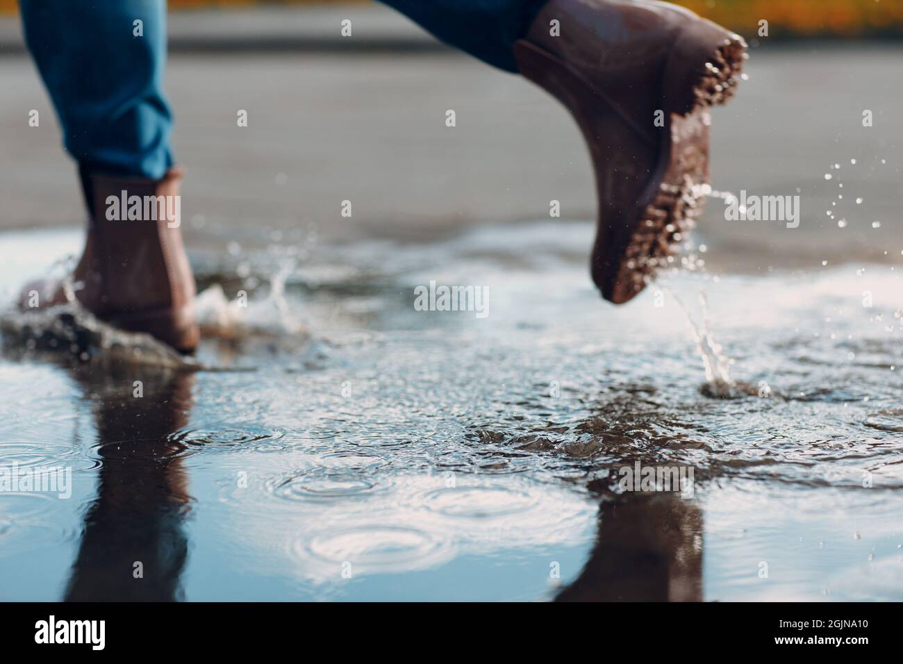Woman wearing rain rubber boots walking running and jumping into puddle with water splash and ...