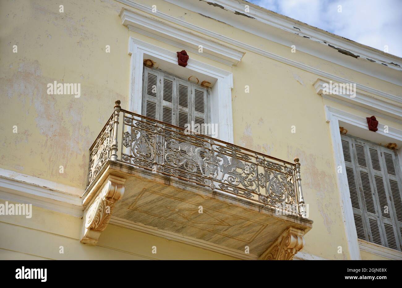 Old Neoclassical house facade with a faded wall, wooden window shutters ...