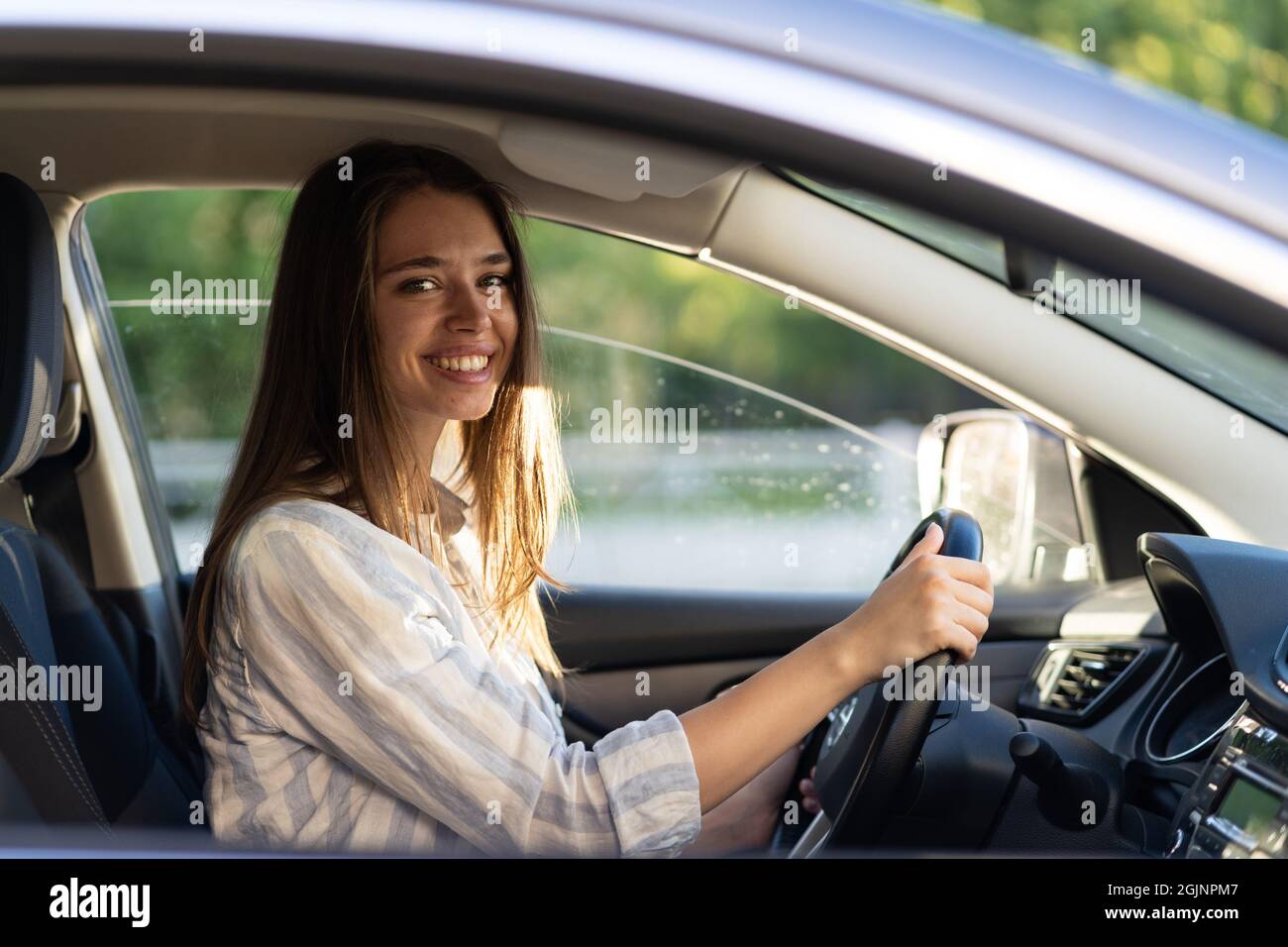 Young girl sit at driver seat in new car smiling hold hands on wheel ...