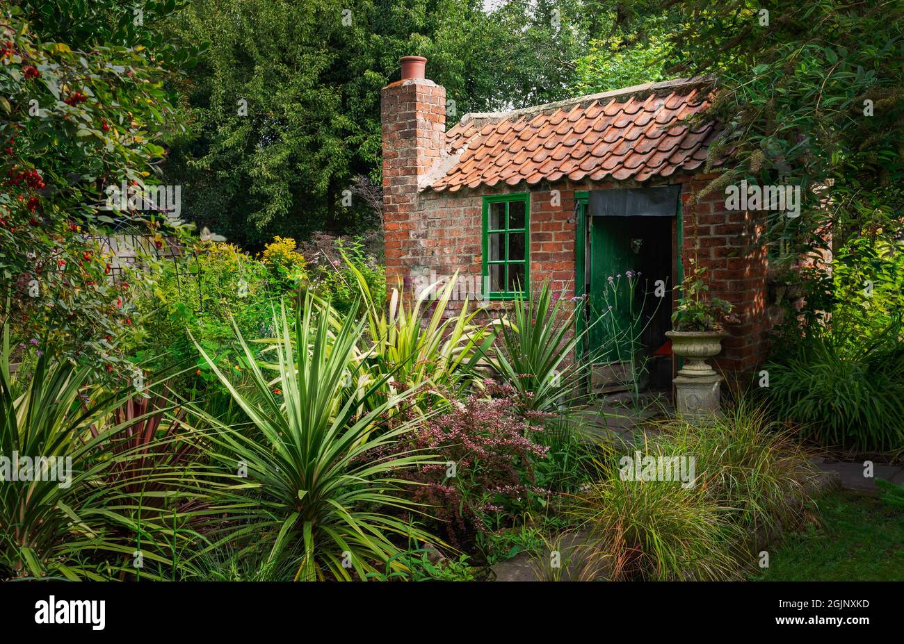 Old traditional summer house surrounded by established shrubs in bloom ...