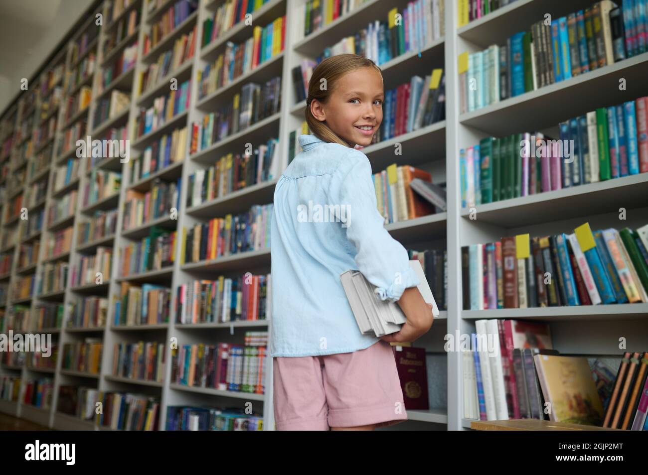 Pleased schoolchild with textbooks looking back over her shoulder Stock ...