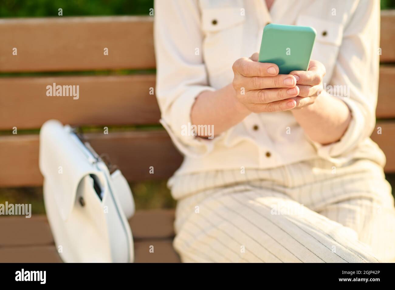 Hands of woman with smartphone sitting on bench Stock Photo - Alamy