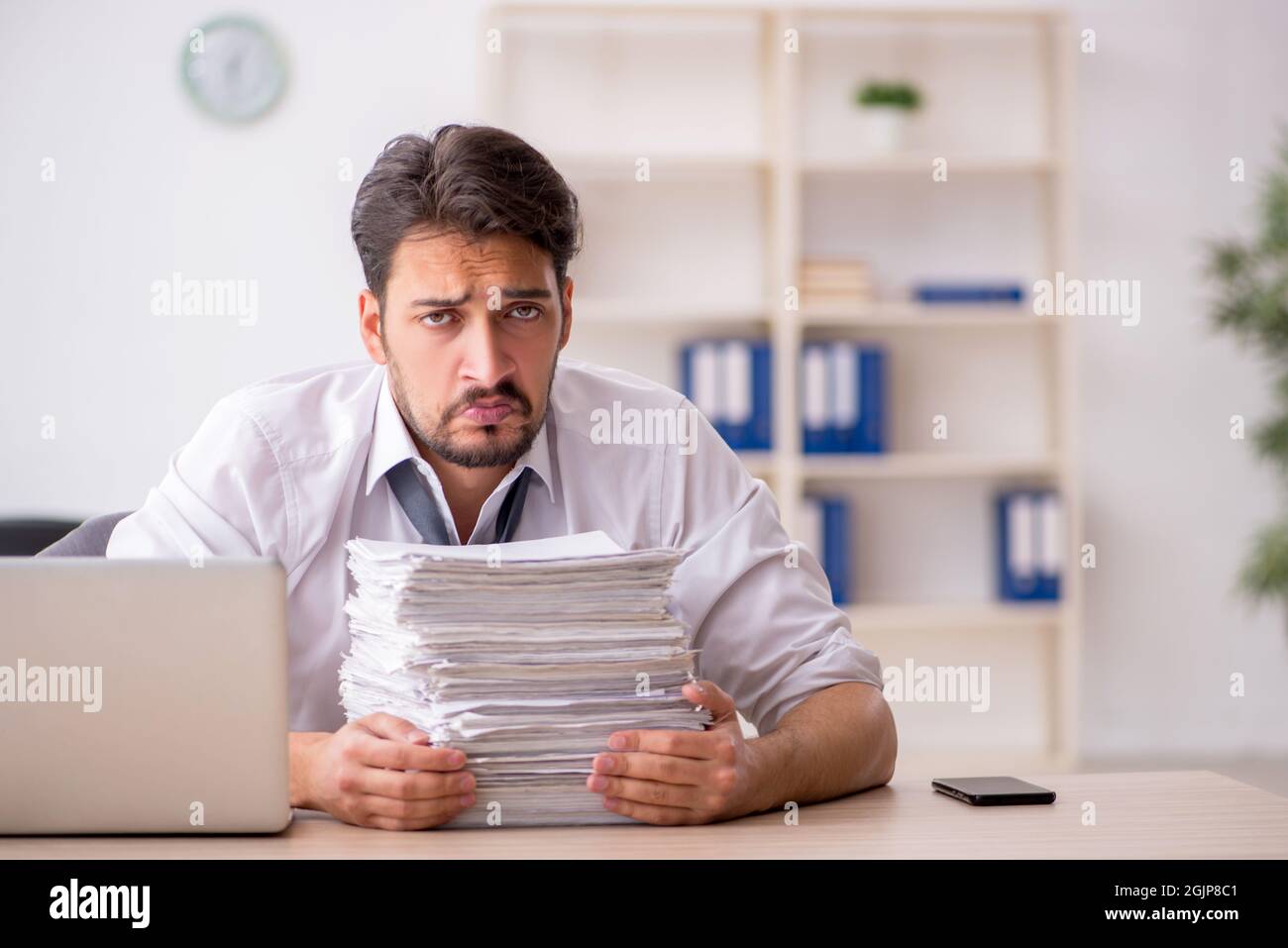 Young male employee and too much work at workplace Stock Photo - Alamy