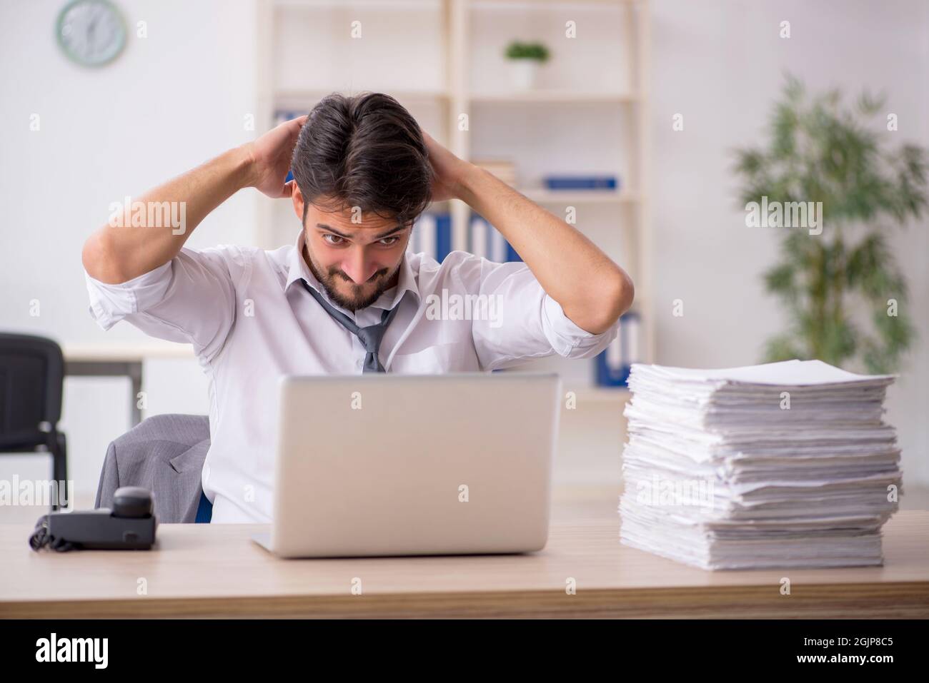 Young male employee and too much work at workplace Stock Photo - Alamy