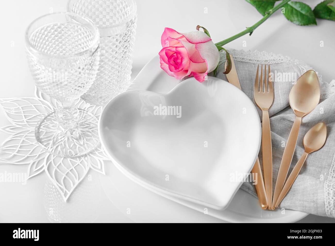 Table setting with plate in shape of heart and rose on light background ...