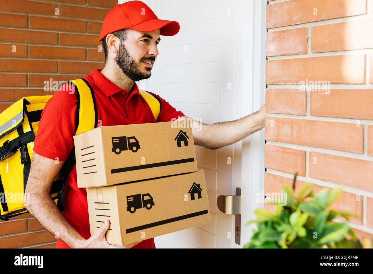 Happy delivery man in red uniform with thermal backpack ringing house ...