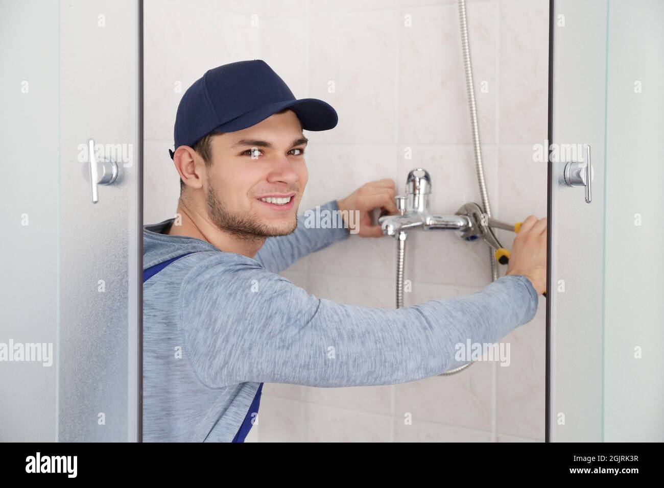 Young handsome plumber fixing faucet in shower stall Stock Photo - Alamy