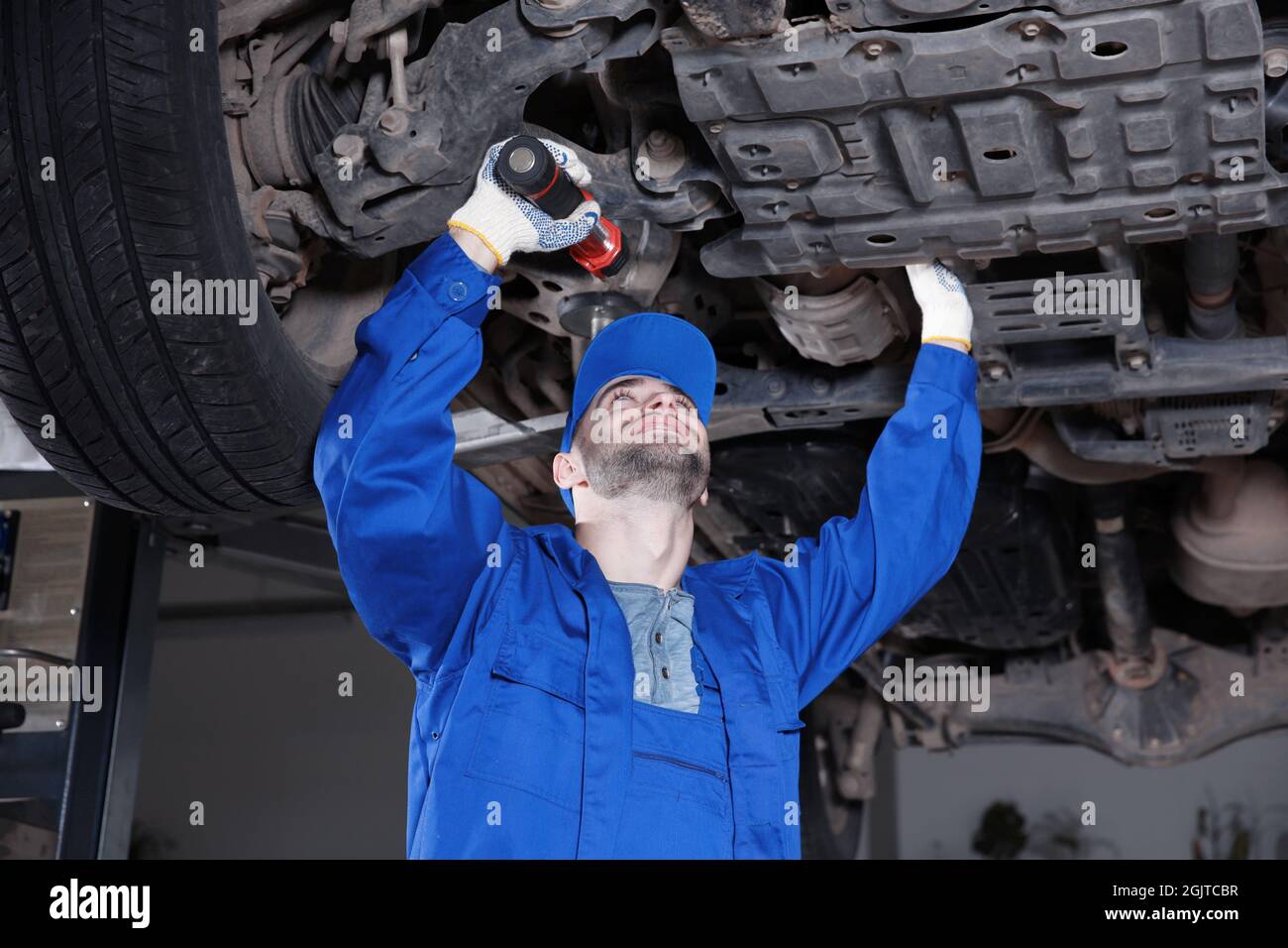 Young mechanic fixing wheel under car in service Stock Photo - Alamy