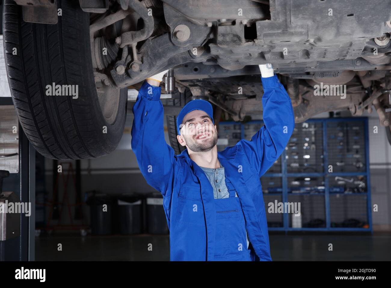 Young mechanic fixing wheel under car in service Stock Photo - Alamy
